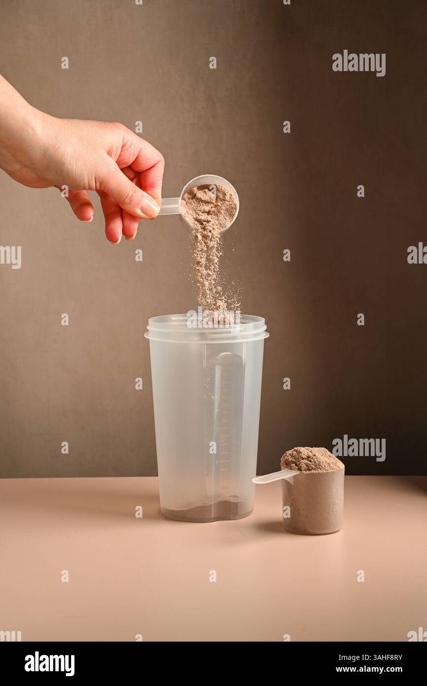 Making protein drink. Pouring chocolate protein powder in a shaker ...