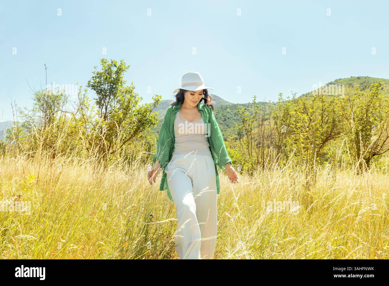 A happy, smiling woman in a white blouse stands in a vibrant meadow ...