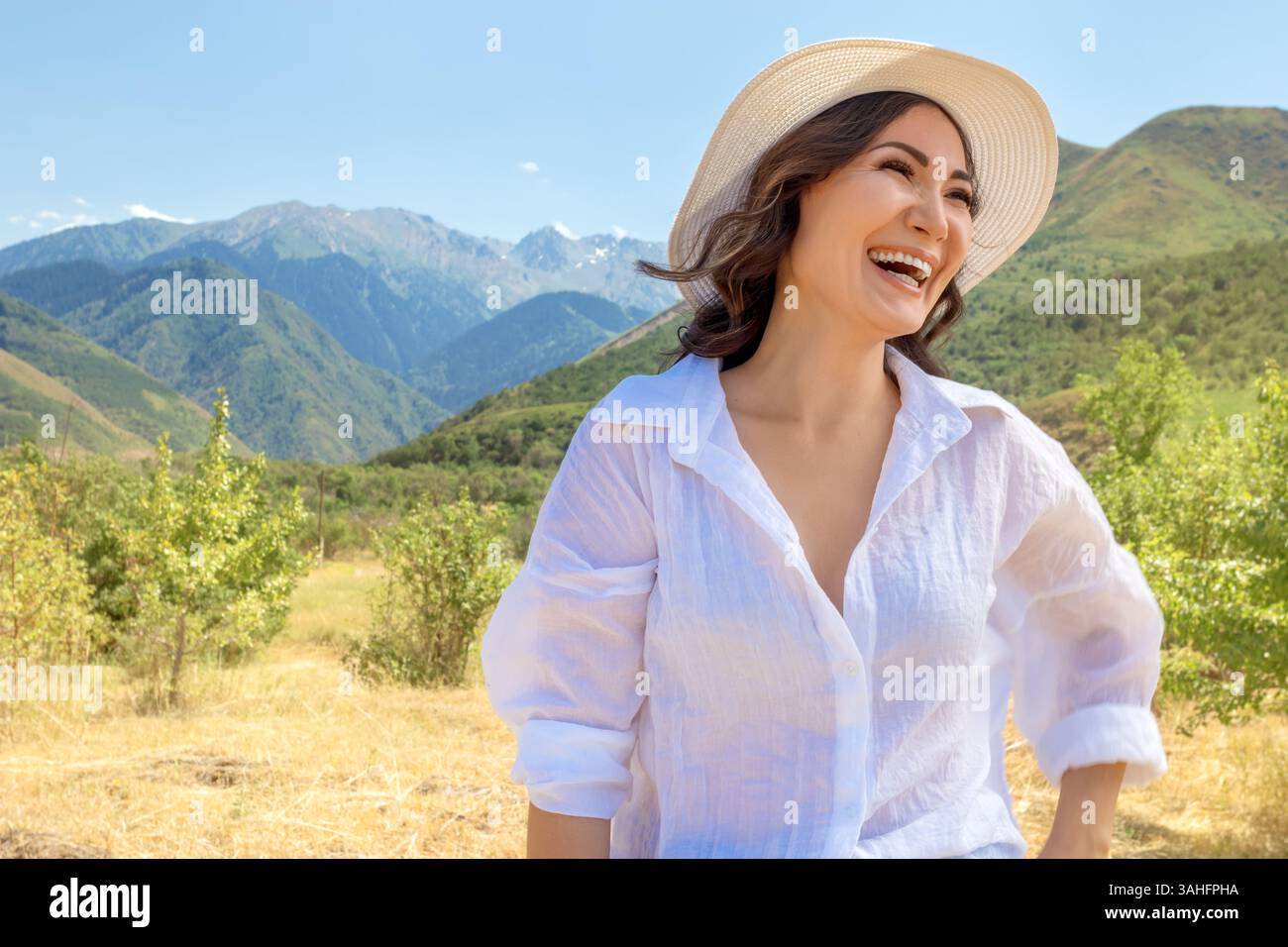 A happy, smiling woman in a white blouse stands in a vibrant meadow ...