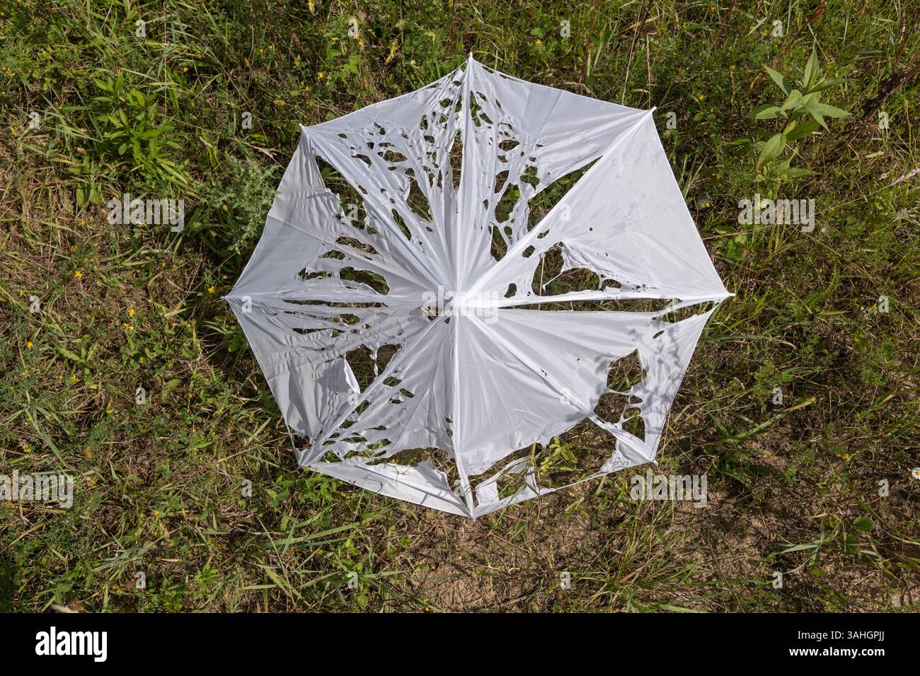 Old and weathered white umbrella with holes, obsolete, damaged and left ...