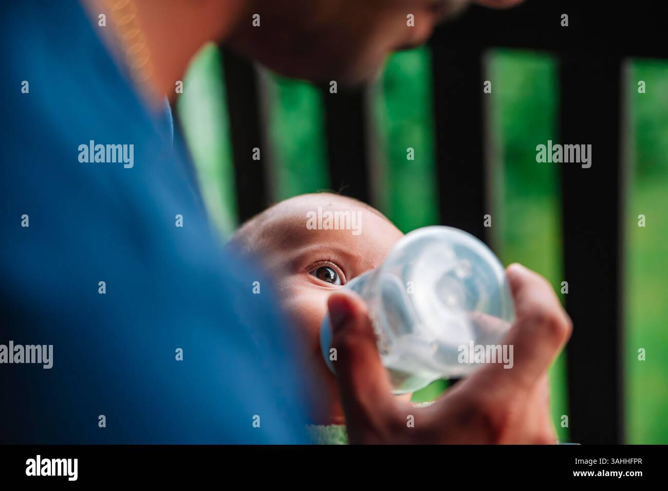 young father giving baby bottle of milk to baby son outdoors. Parenting ...