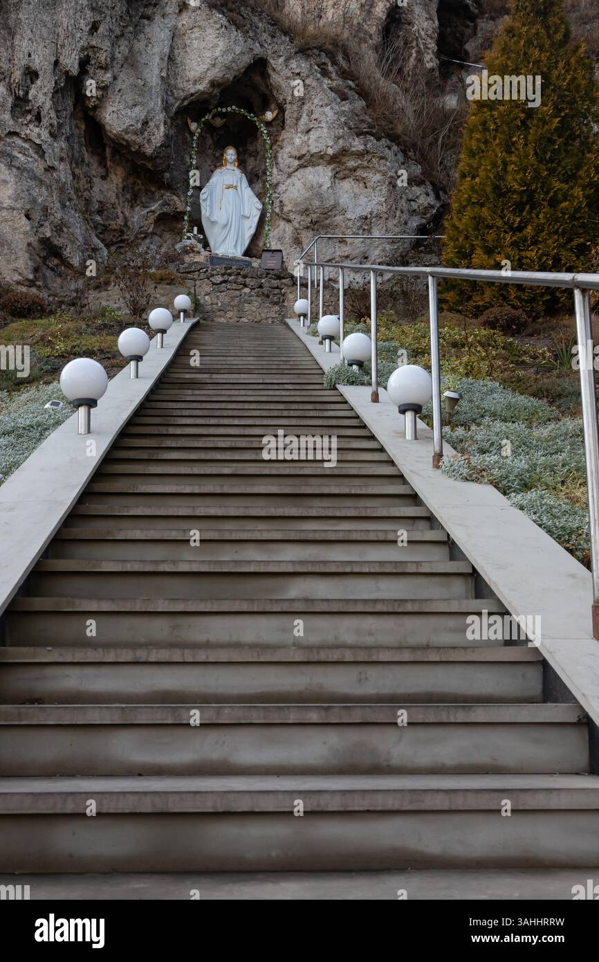 A serene staircase ascends towards a statue located within a cave, framed by natural rocks and ...