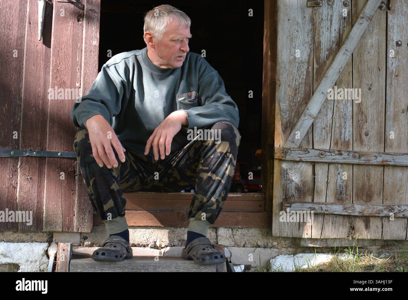 Older man sitting on open barn stairs in village. Senior man spending ...