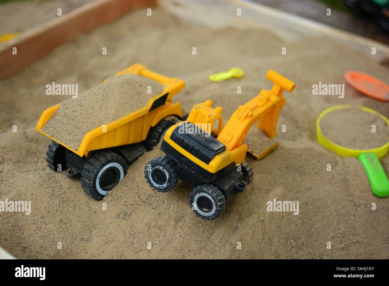 Yellow toy excavator and dump truck digging sand in sandbox. Children ...