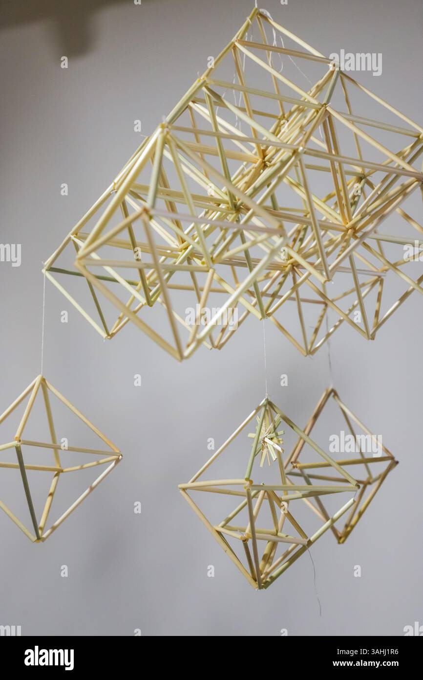 A creative display of geometric shapes crafted from straw sticks hangs ...