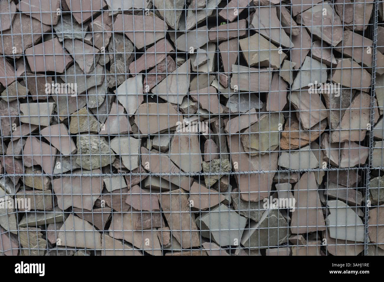 Irregularly shaped stones are arranged tightly within a wire mesh cage ...