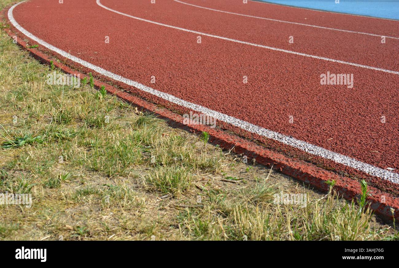 Red running track with grass in left side and blue sports field in ...