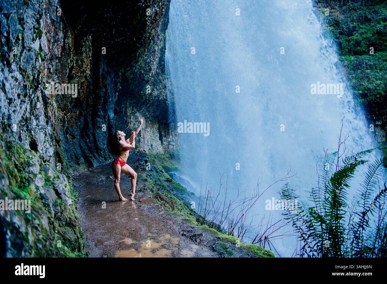 Woman in a red bikini posing near a large cascading waterfall on a ...