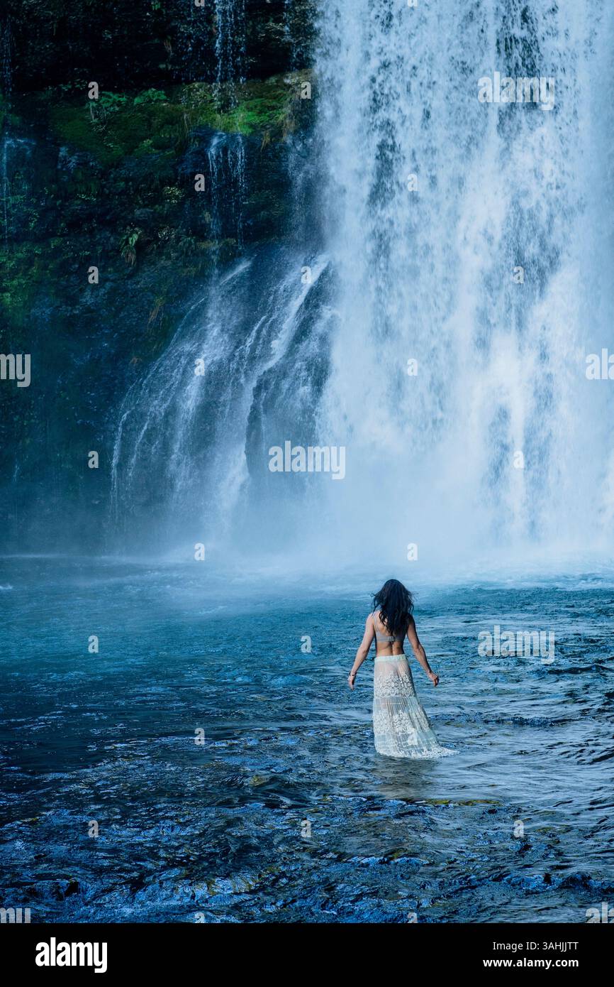 Woman in a white dress standing in front of a powerful waterfall ...