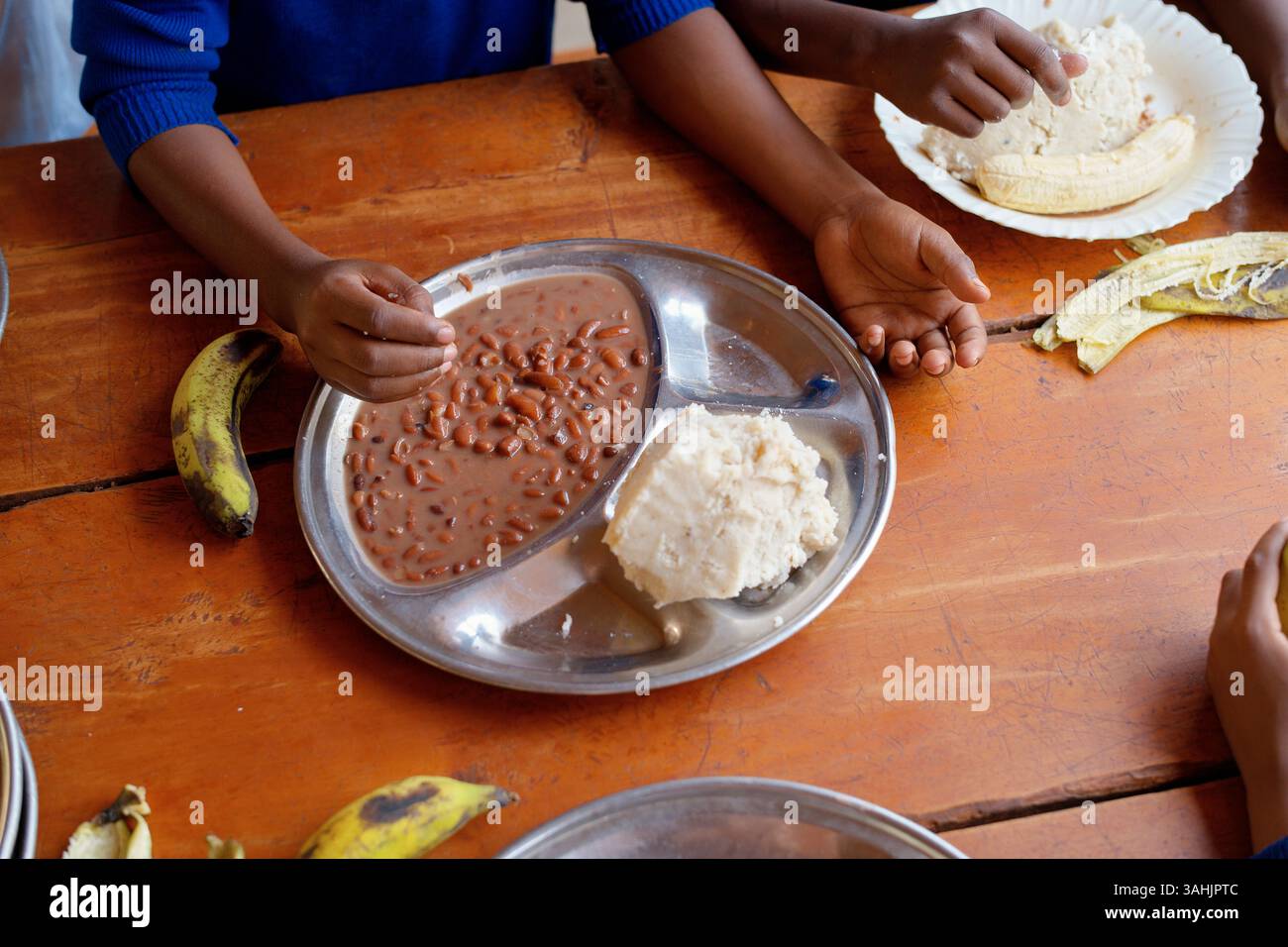 Children eating a meal of red beans, mashed potatoes, and bananas at a ...