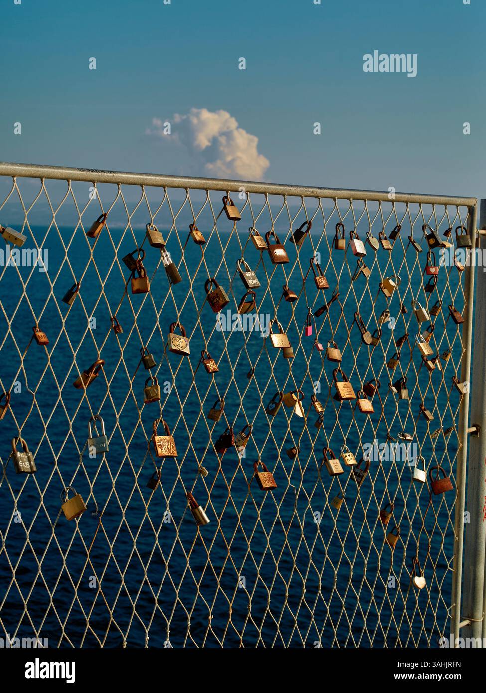 Metal fence over the ocean adorned with numerous padlocks under a clear ...