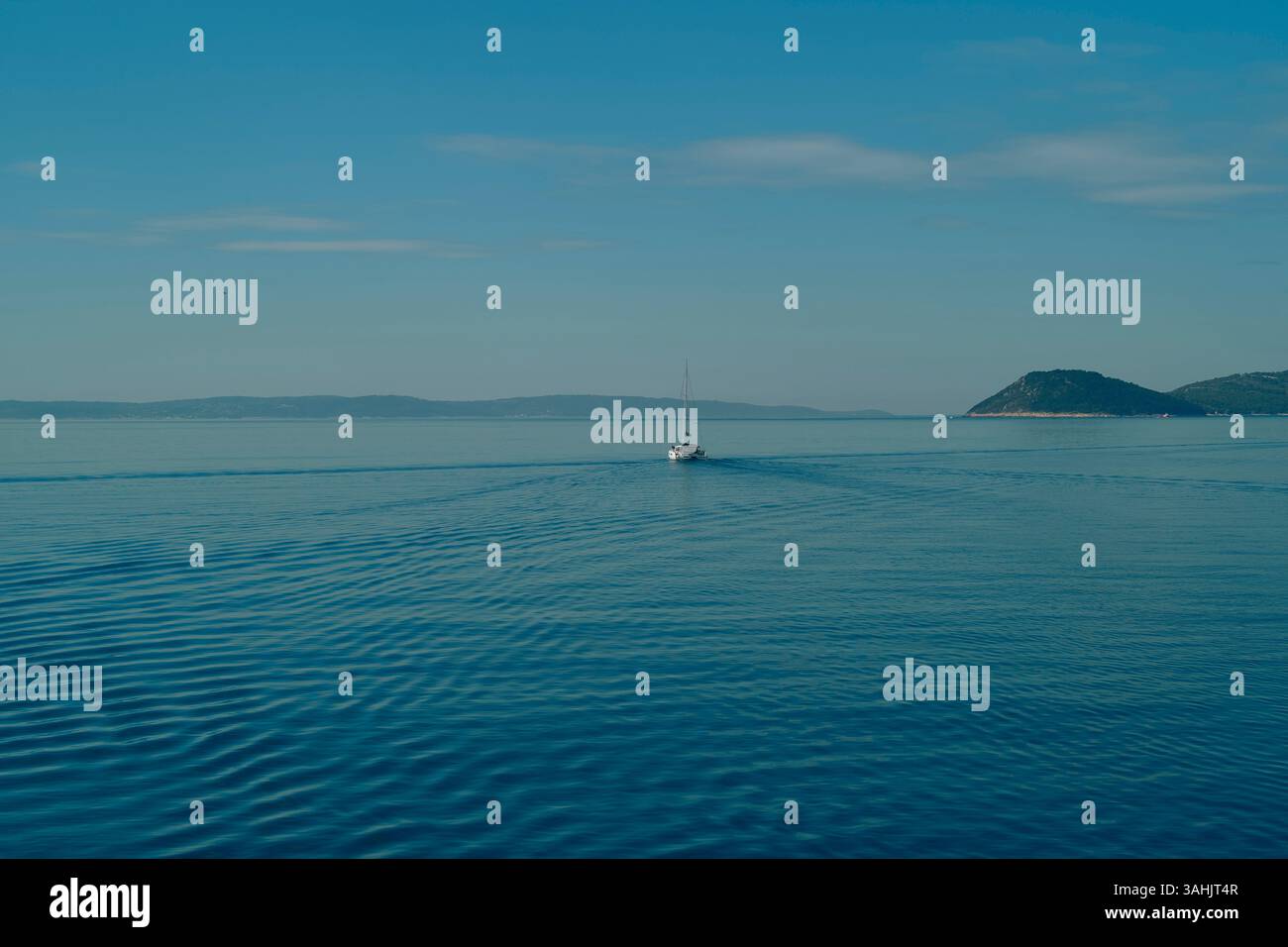 A solitary sailboat glides across calm blue ocean waters under a clear ...