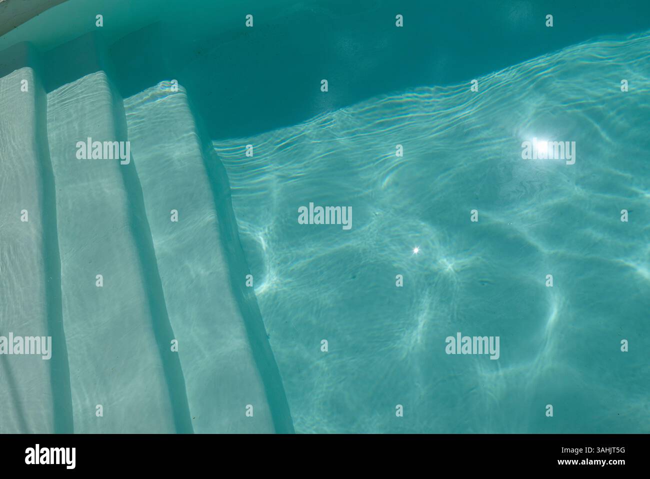 Sunlight refracts in a clear blue swimming pool with visible white ...