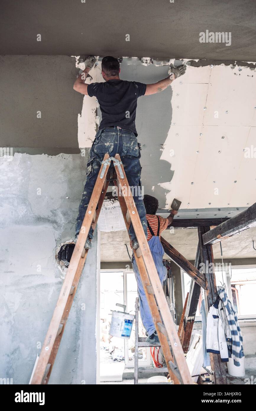 Male builder at work overalls plastering and restoring old wall using a ...
