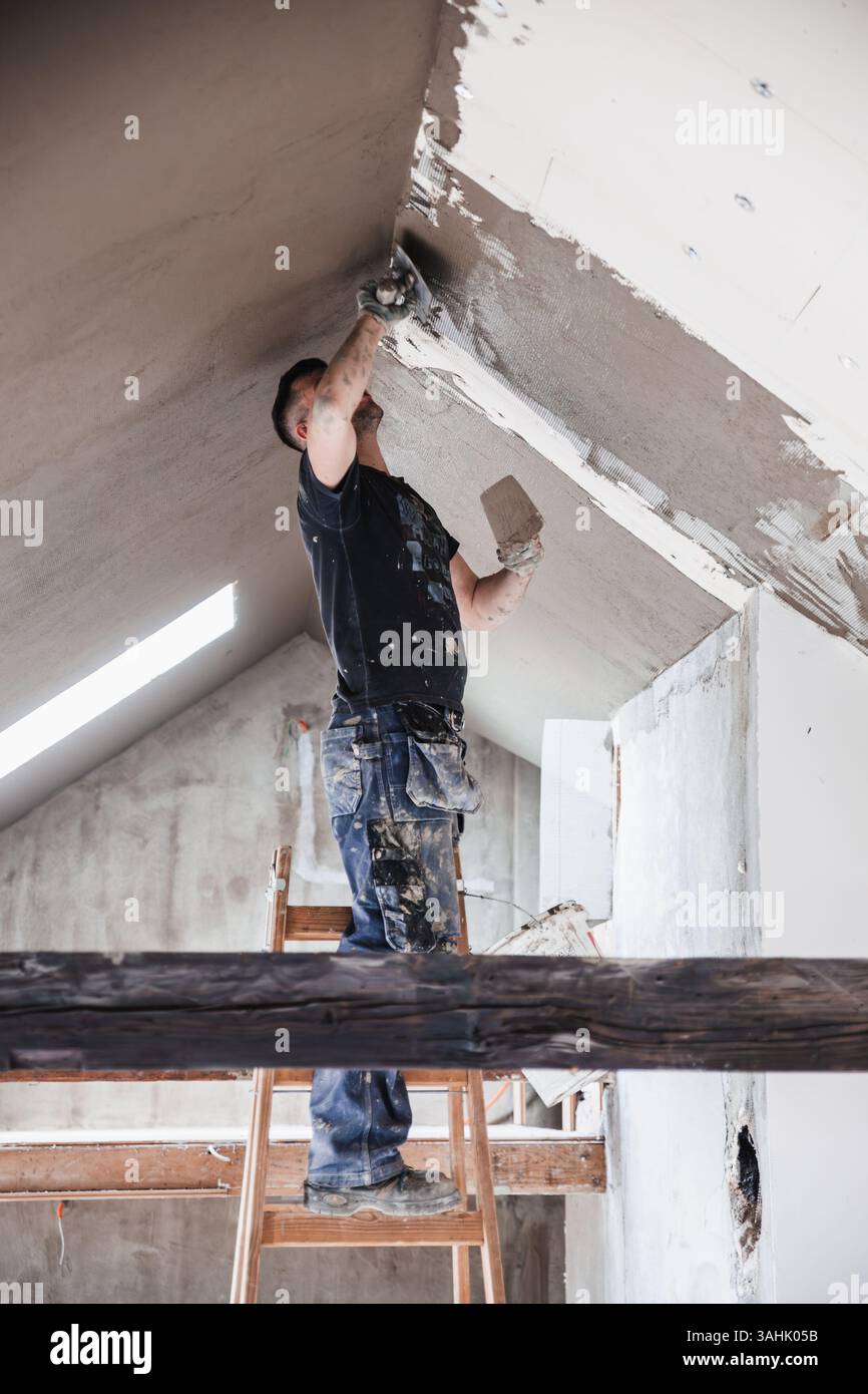 Male builder at work overalls plastering and restoring old wall using a ...