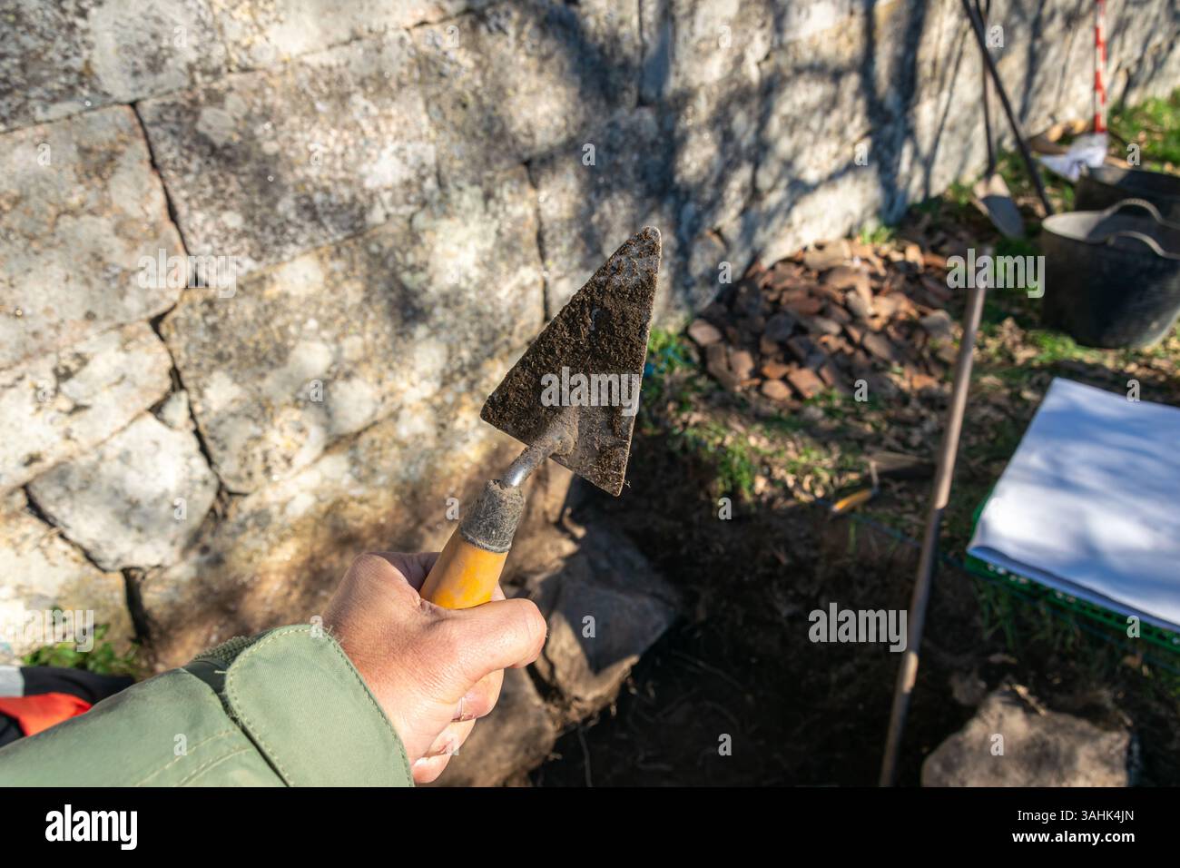 an archaeologist holds a trowel in their hand at an archaeological dig ...