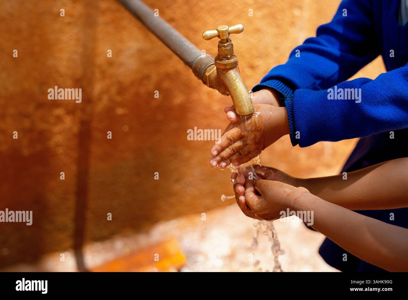 Two children washing hands under a water tap outdoors on a sunny day ...