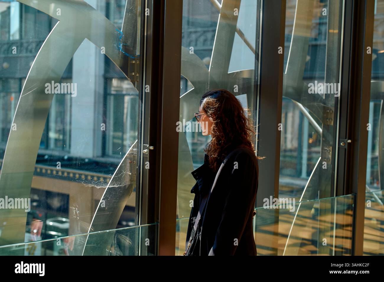 Woman with curly hair gazing out a window in a modern glass building ...