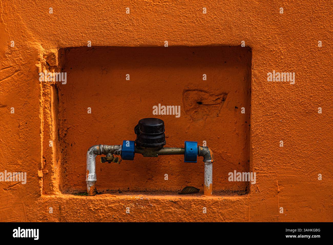 Water meter embedded in an orange wall with exposed pipes and a vivid ...