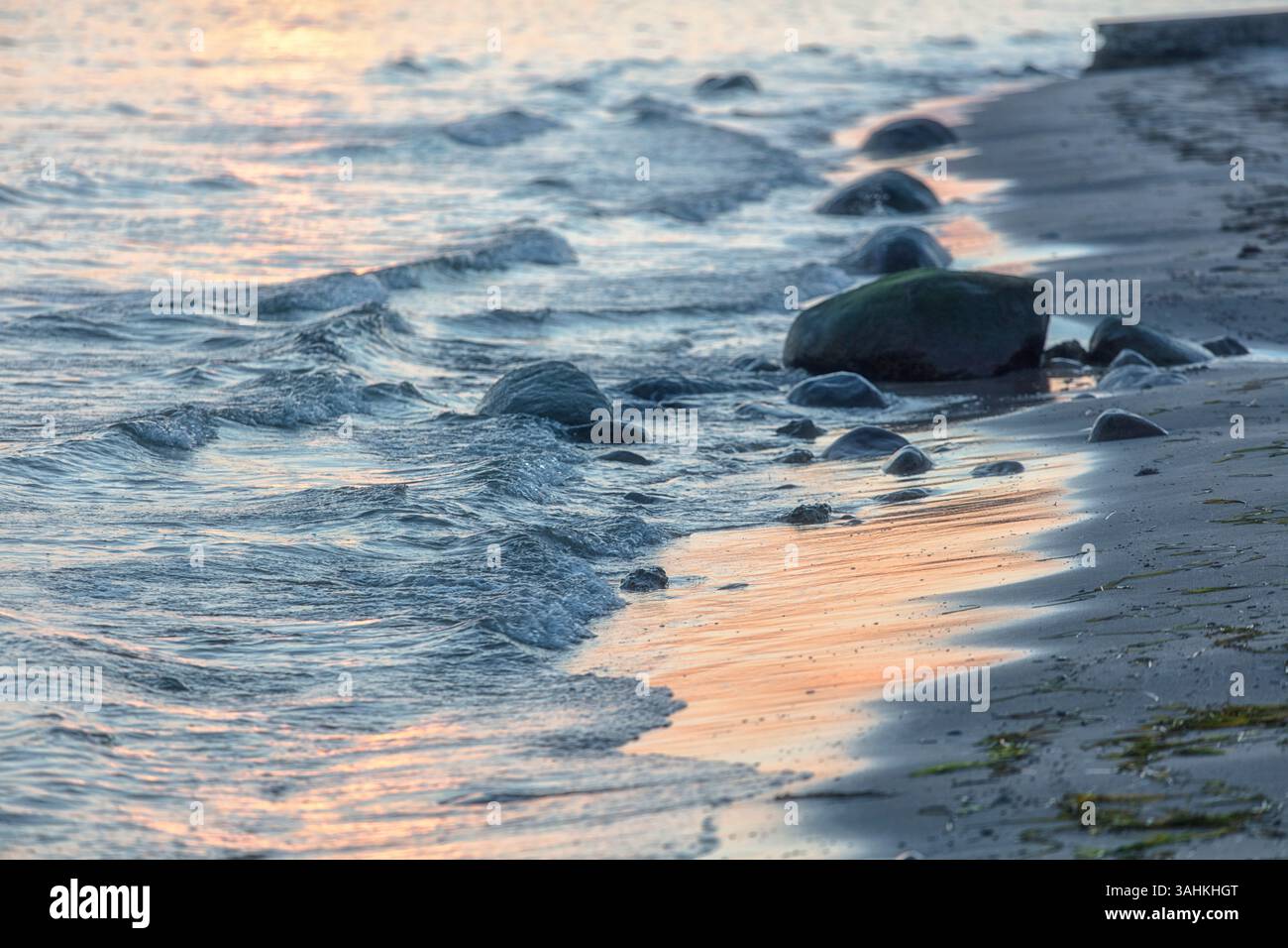 Gentle waves lap against a sandy shore, reflecting soft pastel colors ...