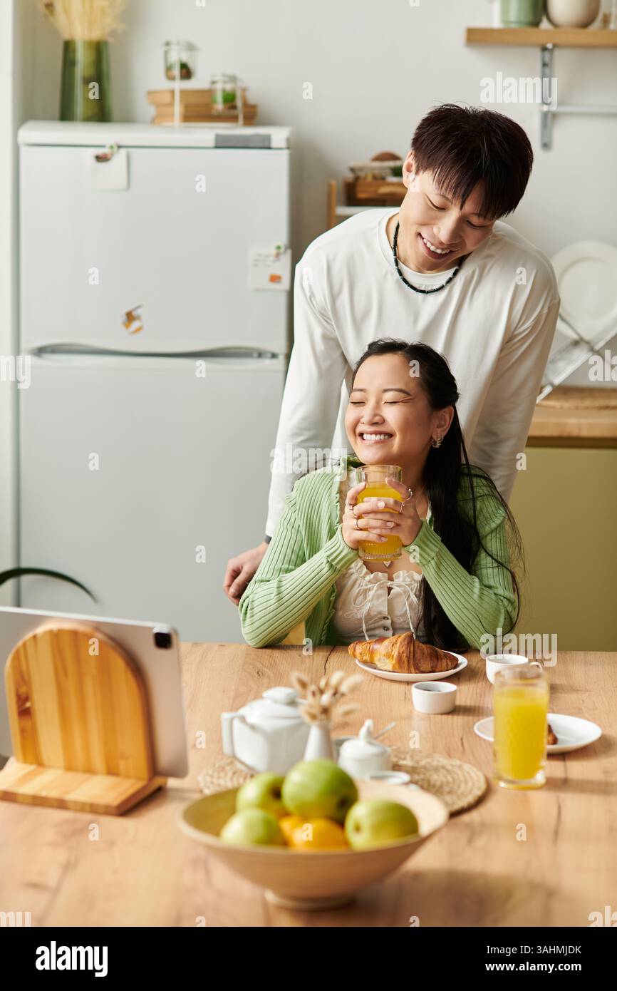 A young Asian couple enjoys a cheerful breakfast, laughing and sharing ...