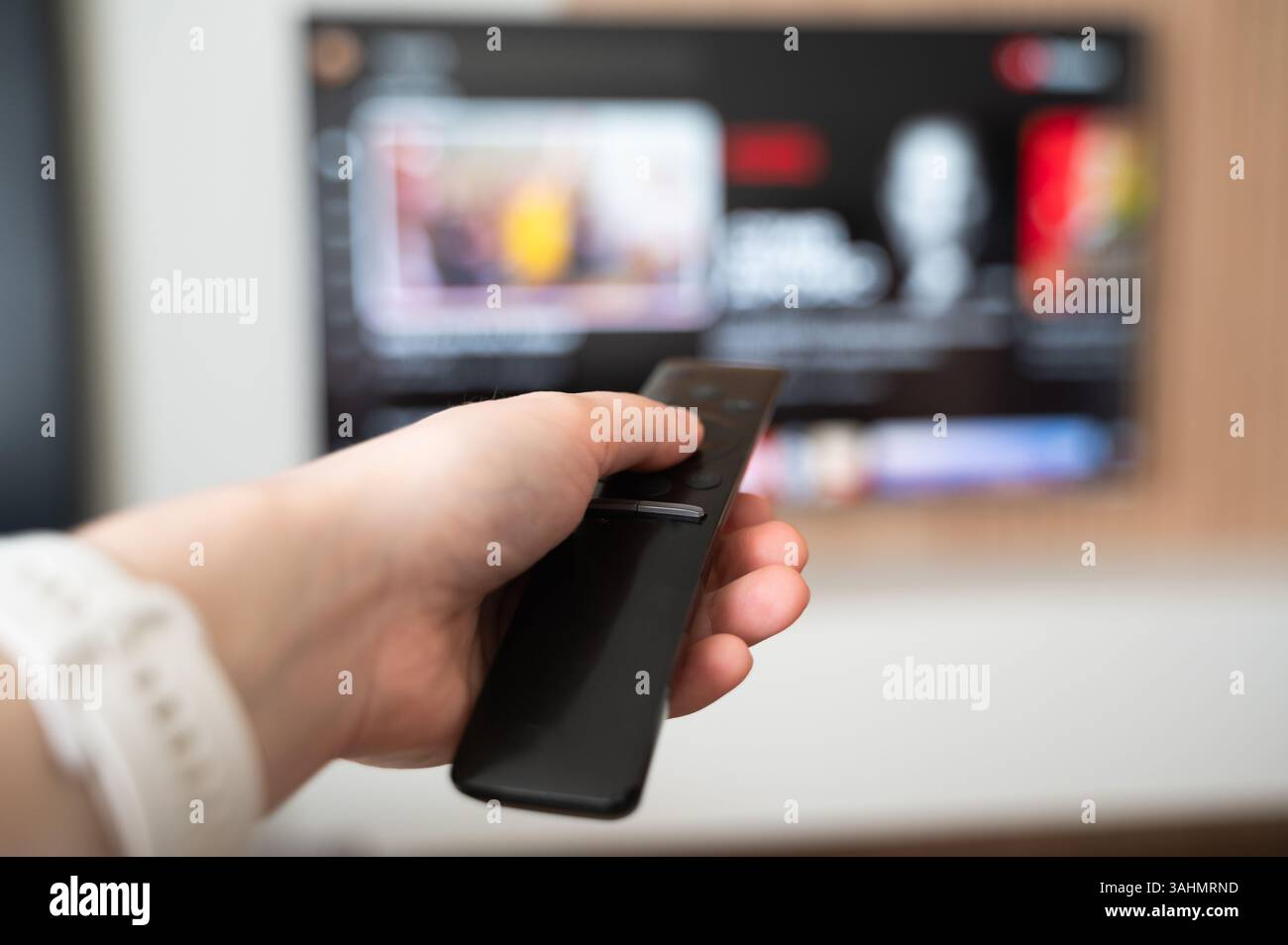 A person is sitting comfortably and holding a remote control while ...