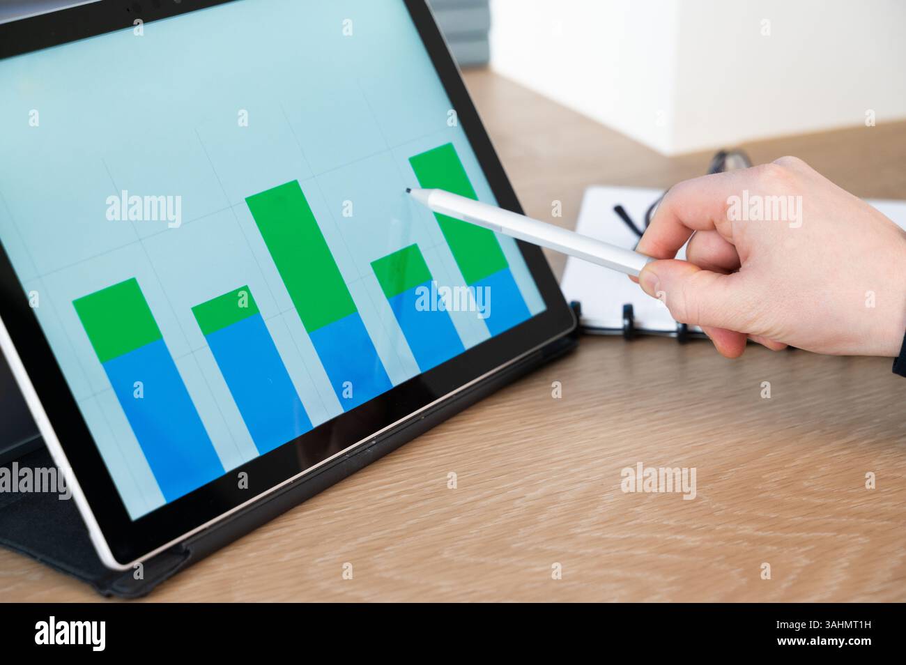 A skilled professional analyzes data trends on a tablet with a stylus ...