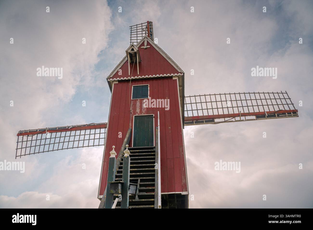 A charming red windmill stands tall against a cloudy sky, showcasing ...