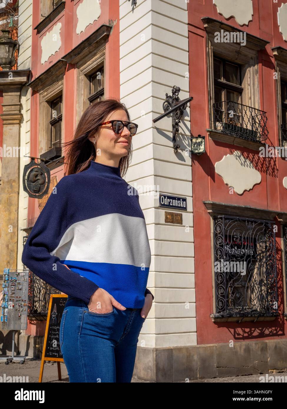A woman in a blue and white striped sweater stands by a building in ...