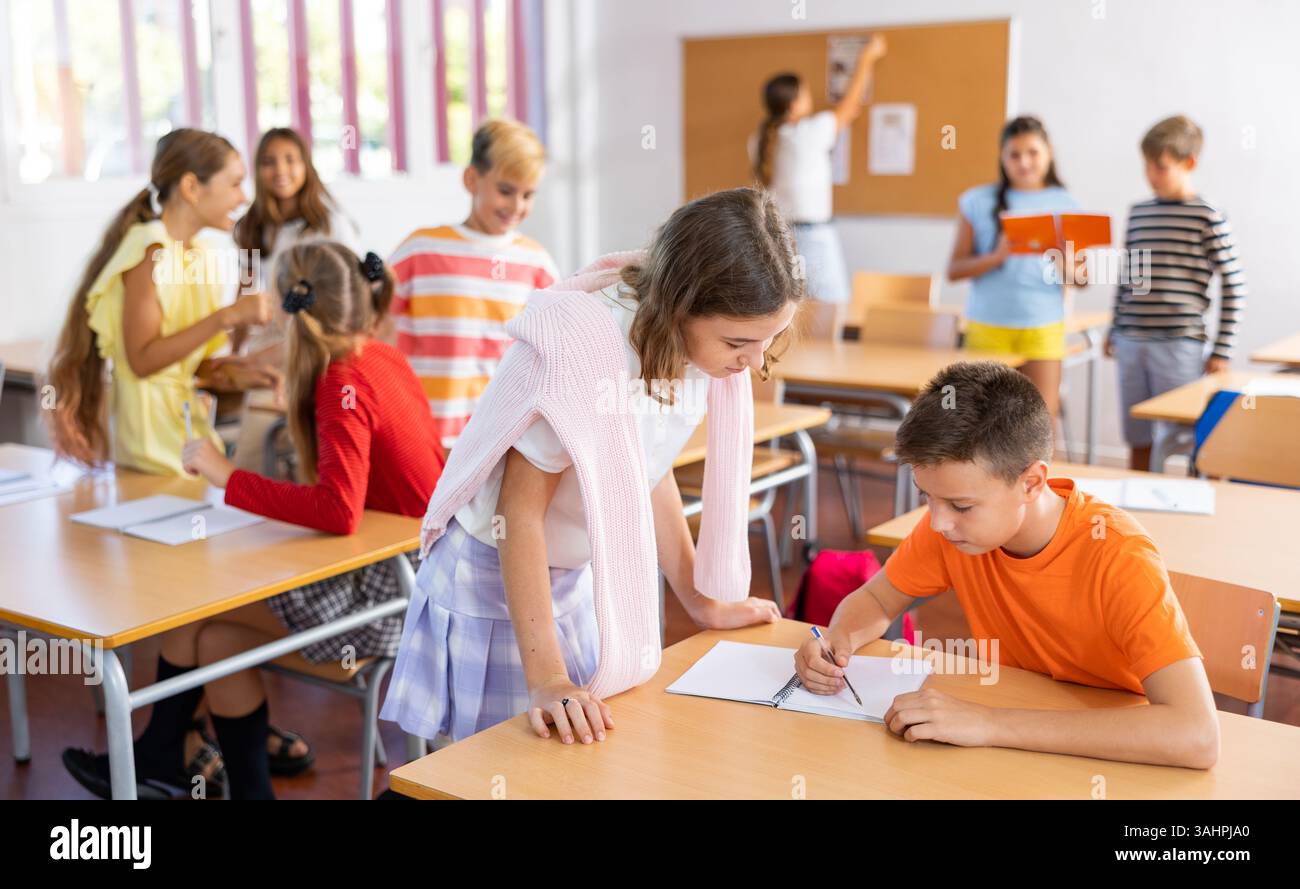 Tween girl helping classmate to complete written assignment in class ...