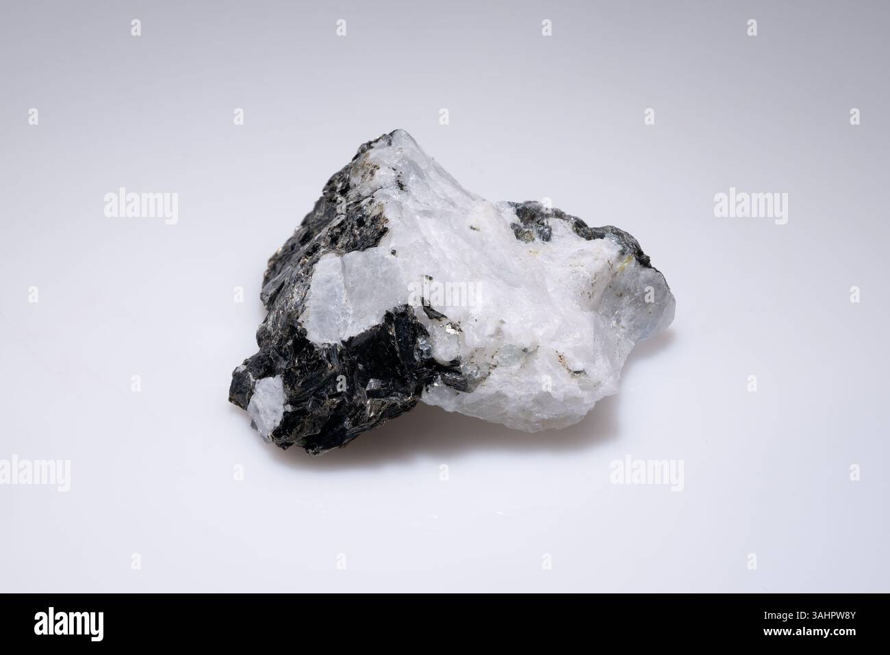 Raw moonstone specimen with black inclusions against a plain white ...