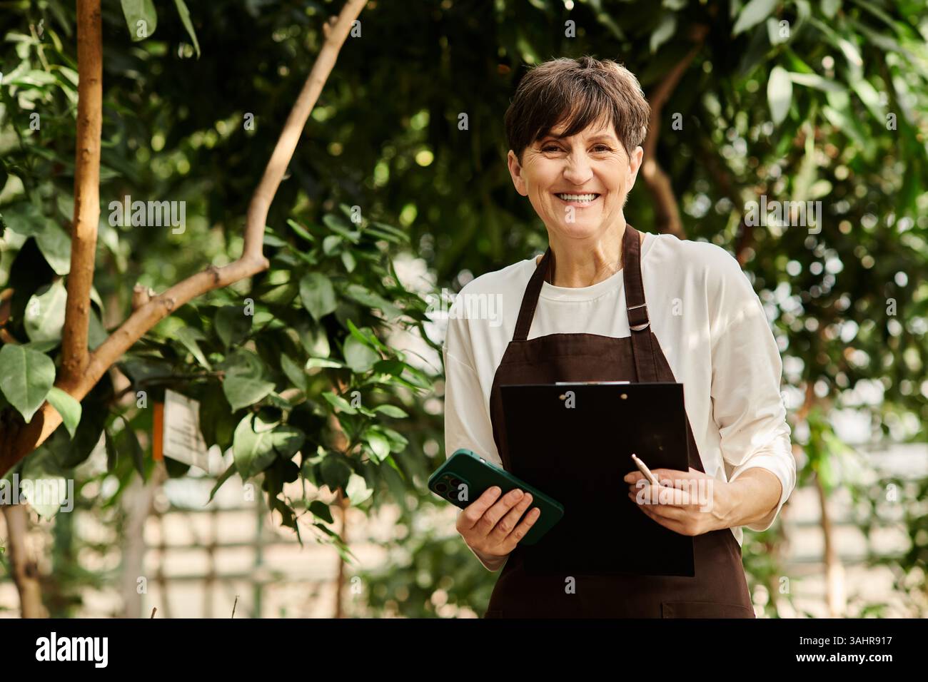 Mature woman stands proudly in a greenhouse, smiling as she manages her ...