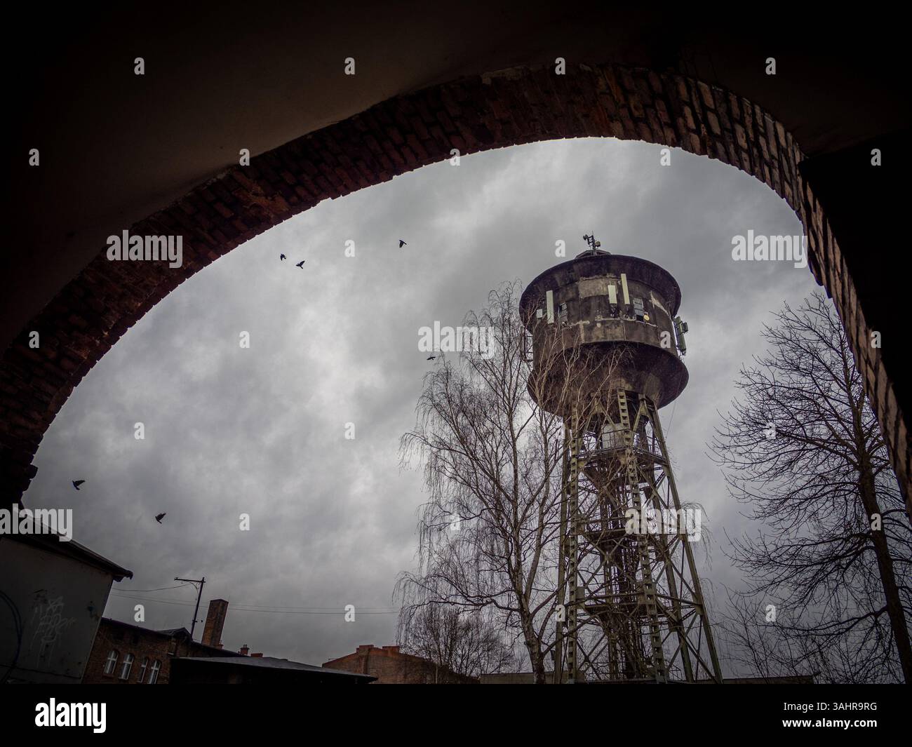 A tall water tower can be seen prominently through a brick archway in ...