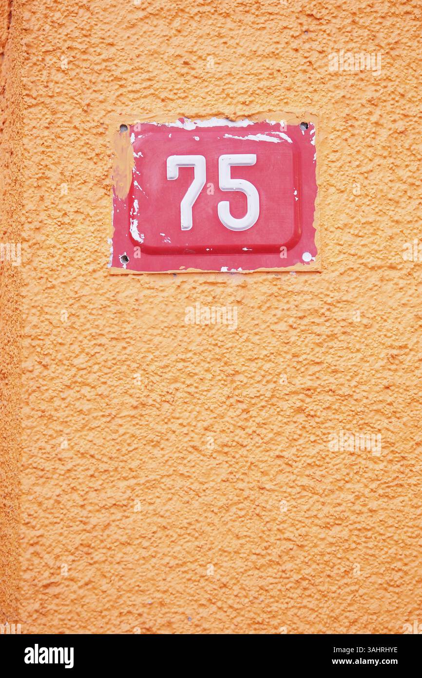 Numeric house number 75 displayed on vibrant orange wall Stock Photo ...