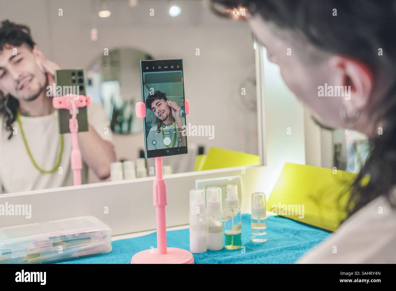 Young non-binary hairdresser recording a makeup tutorial video with a smartphone on a tripod ...