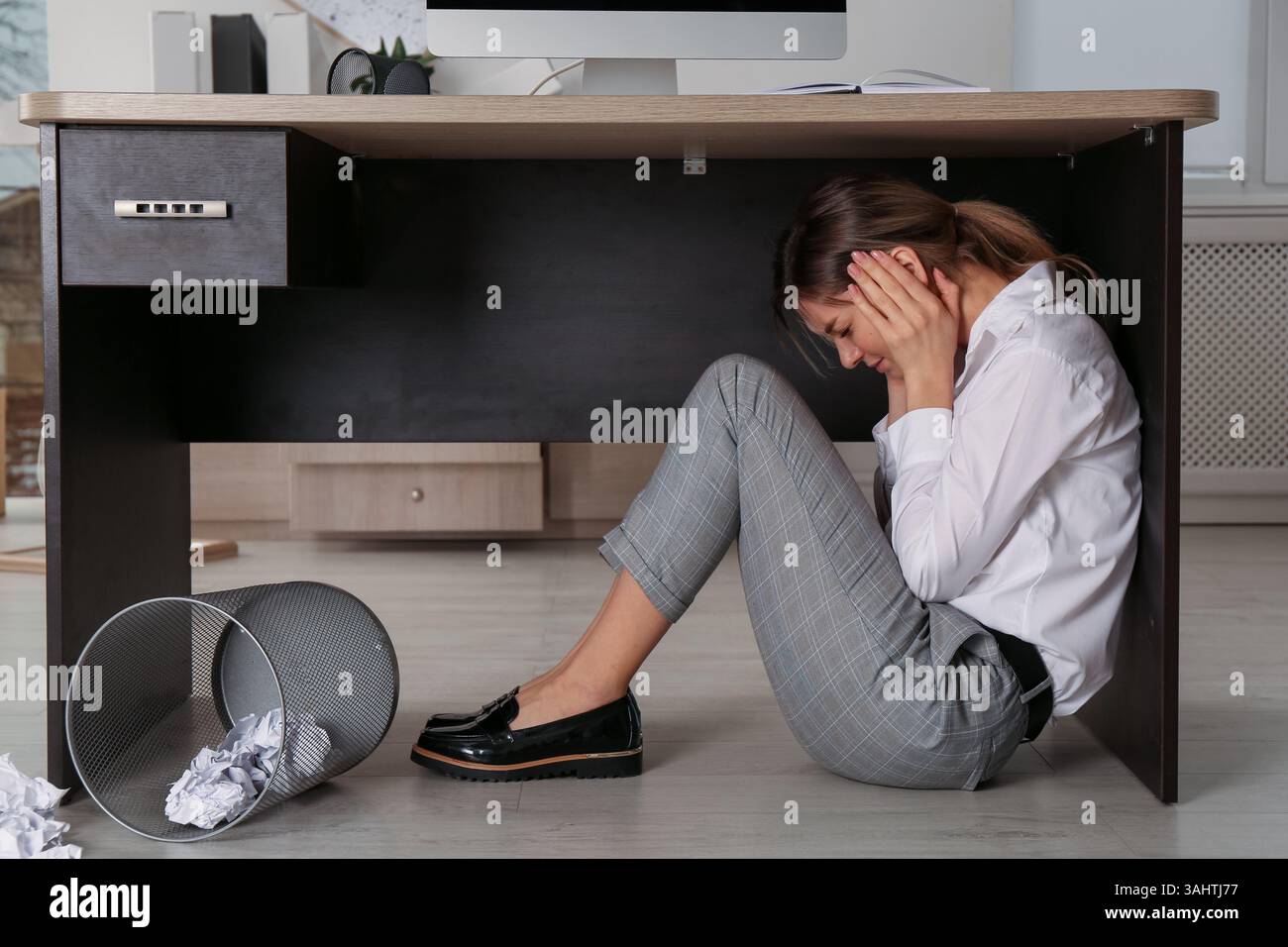 Scared young woman hiding under office desk during earthquake Stock ...
