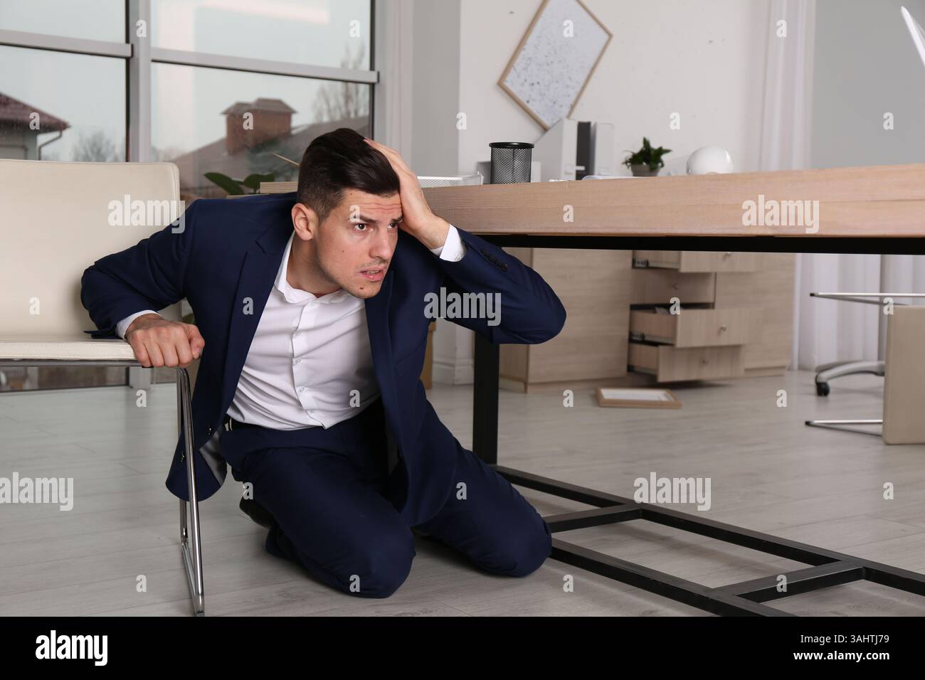 Scared man on floor near office desk during earthquake Stock Photo - Alamy