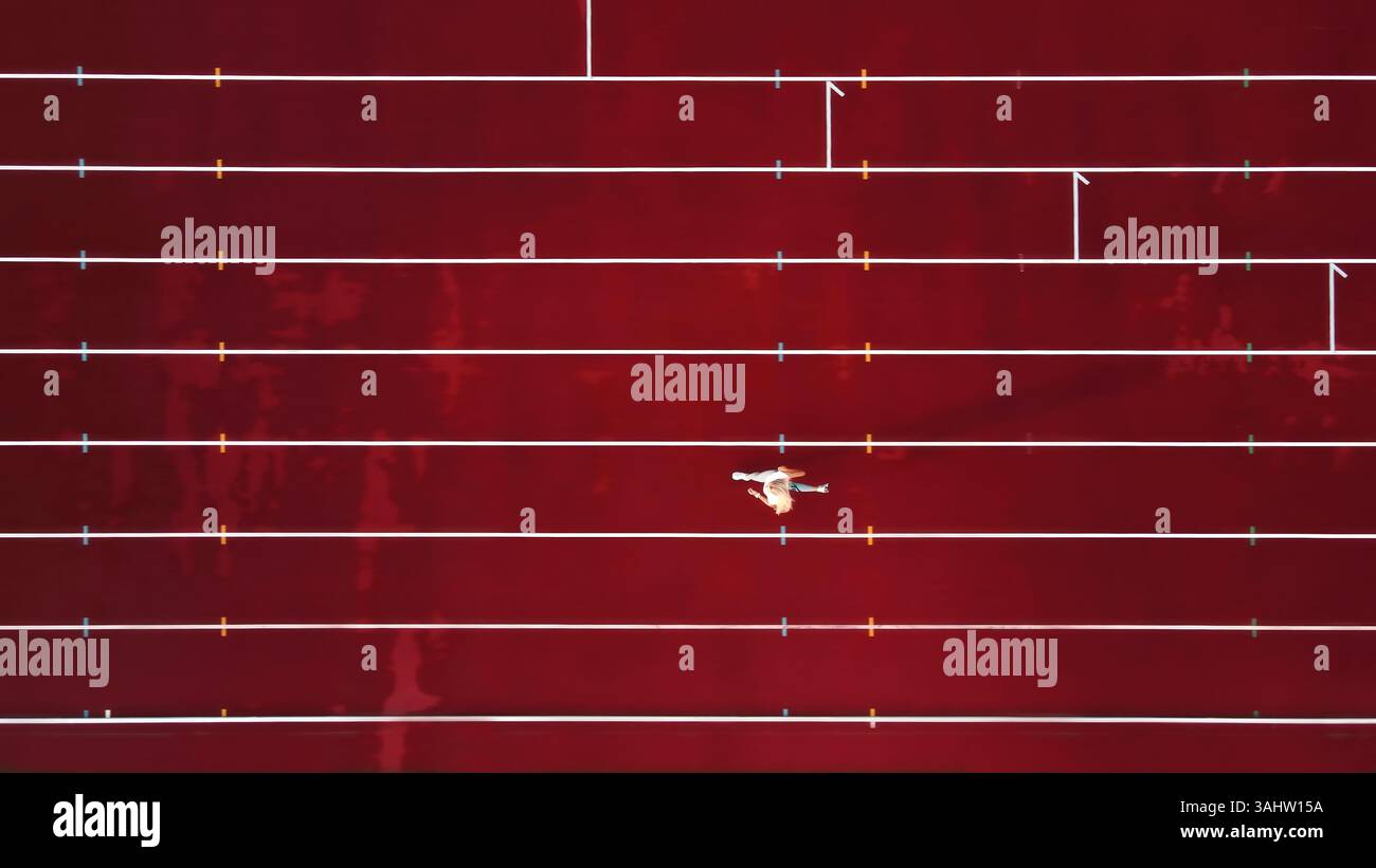 Aerial view of athlete on red track field. A lone athlete runs on a ...