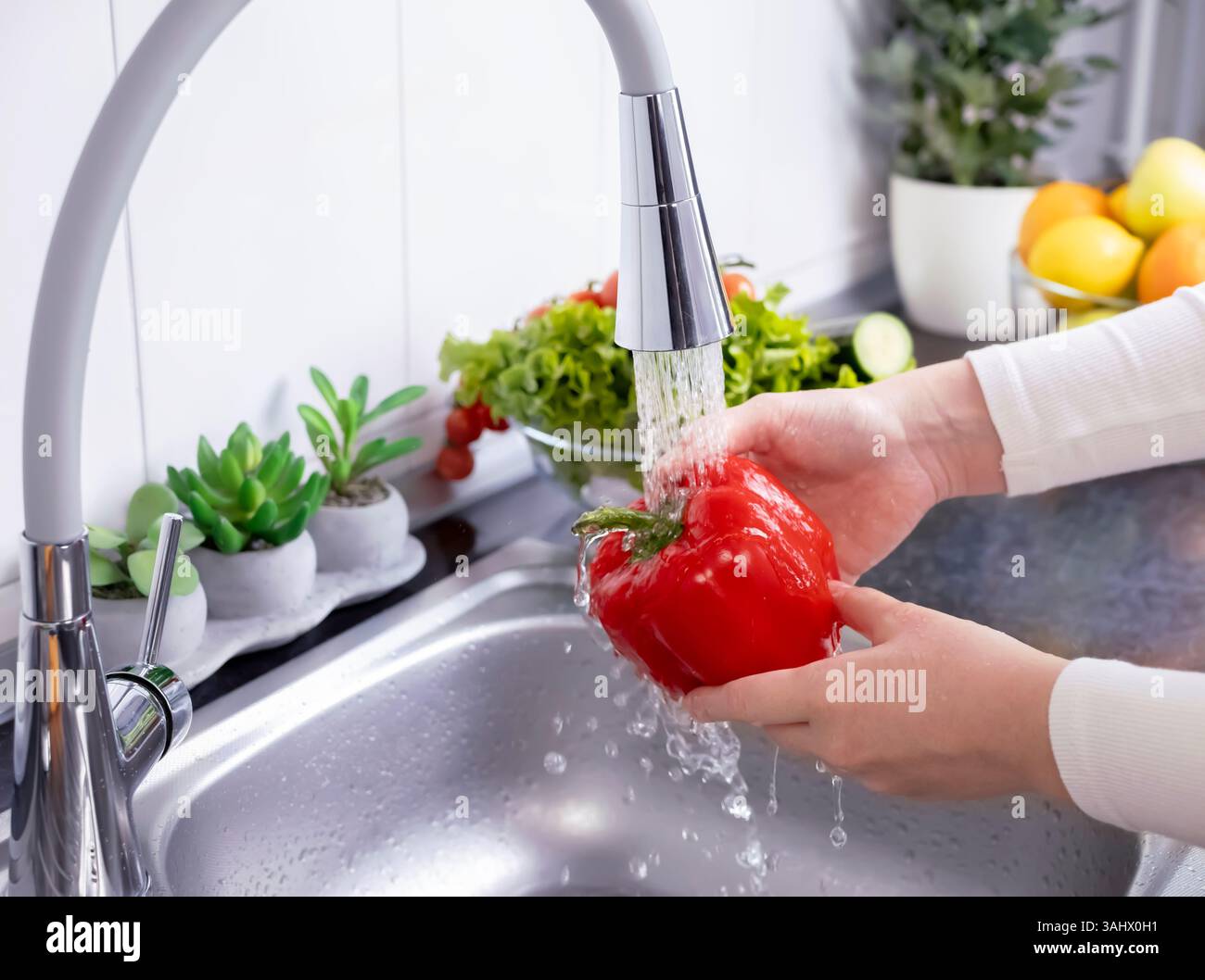 Woman hands washing a red bell pepper to prepare a fresh salad in the ...