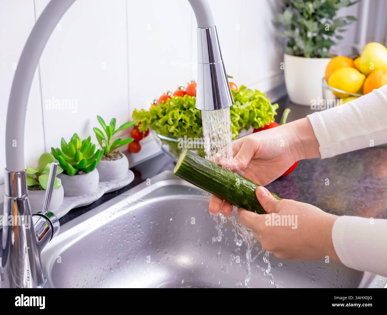Woman hands washing a cucumber to prepare a fresh salad in the kitchen ...