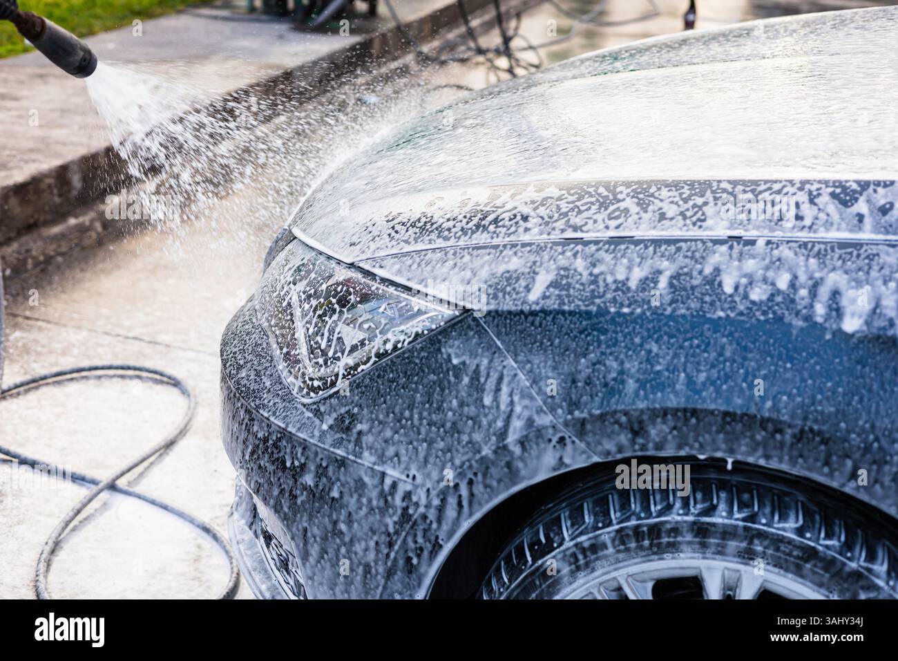 A vehicle covered in soapy foam is being cleaned at an auto detailing ...