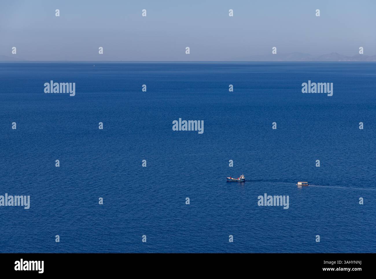 A picture of a boat dragging a barge in the blue of the Aegean Sea ...