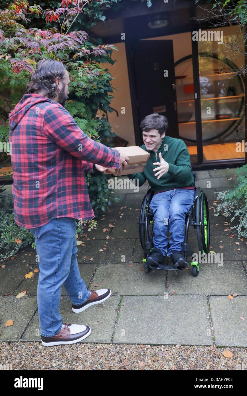 Man giving cardboard box to man in wheelchair in front of house Stock ...