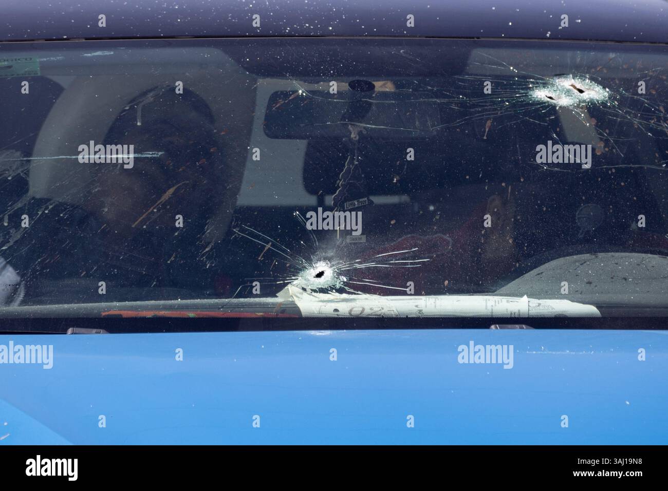 A bullet-riddled windshield of a blue car involved in a crime scene ...