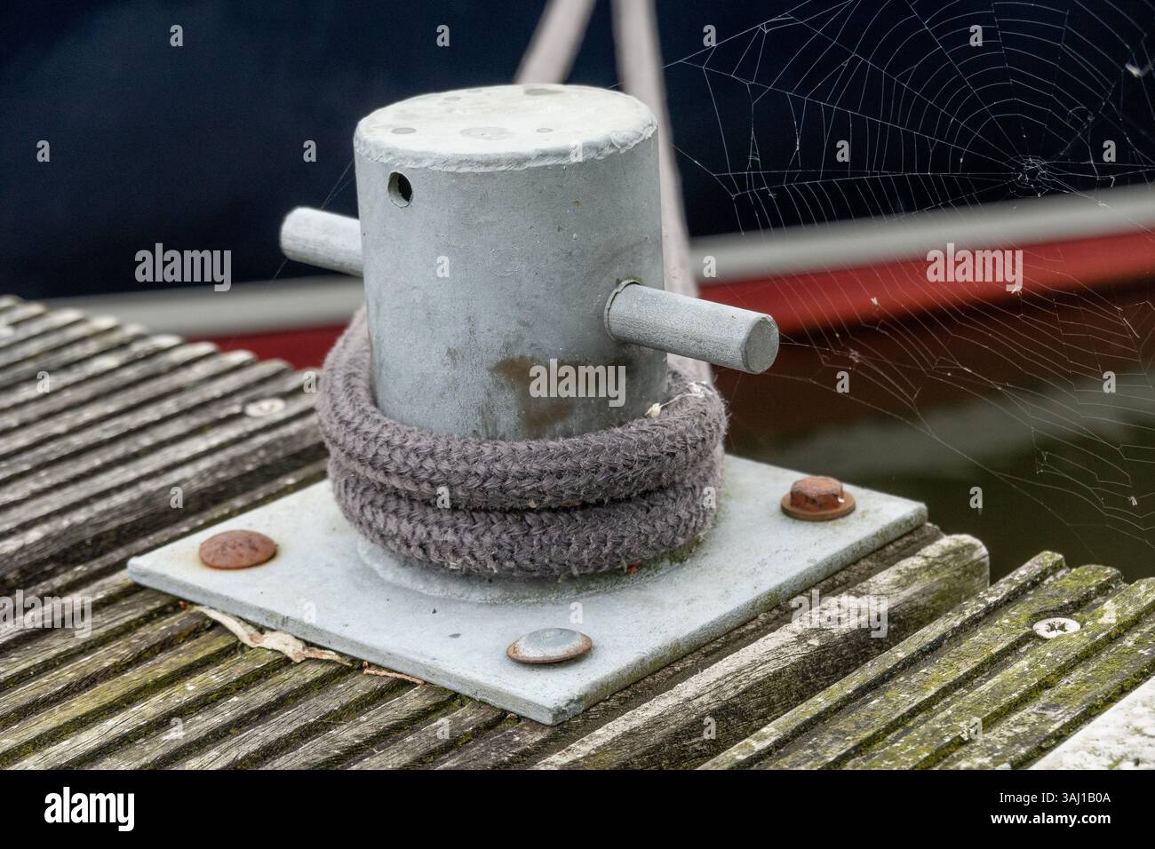 A metal bollard sits on a weathered wooden dock, surrounded by a coiled ...