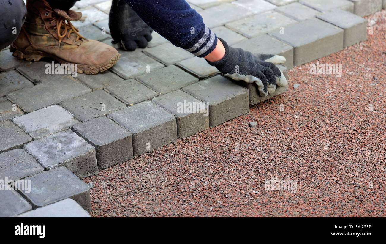 Worker Laying Concrete Pavers on Gravel. Close-up of a worker aligning ...