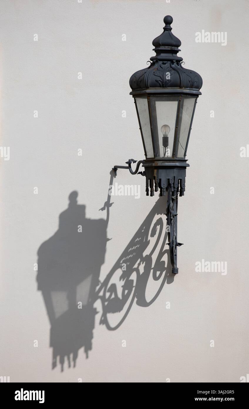 An old gas lamp fixed on a white wall, its shadow is posed on the wall ...