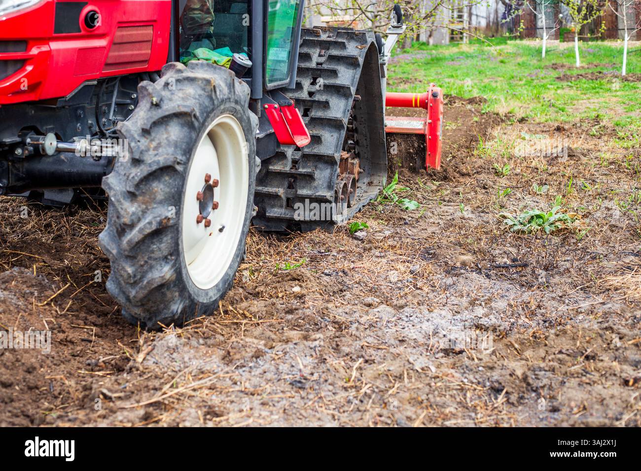 A caterpillar tractor mills the soil in a rural field. Plowing a summer ...
