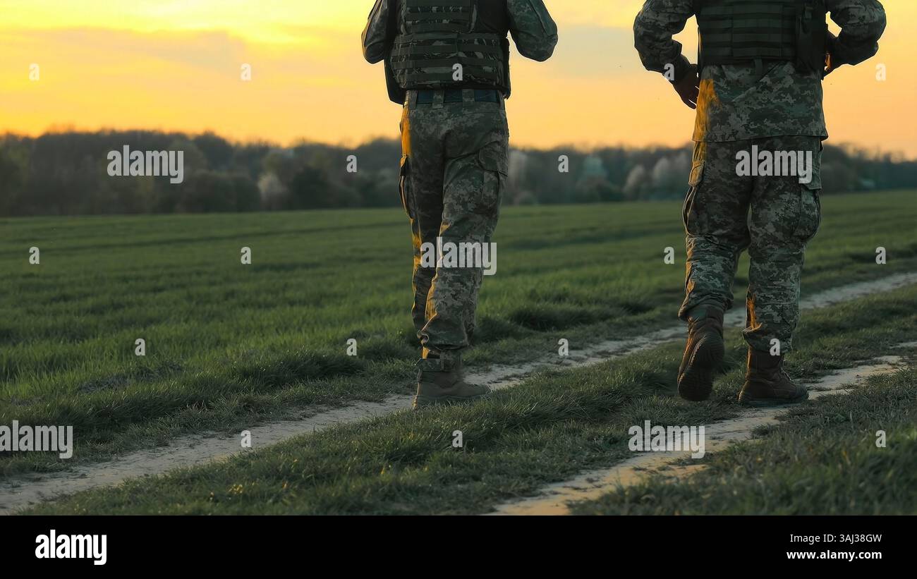 Soldiers walking through field at sunset. Two soldiers in camouflage ...