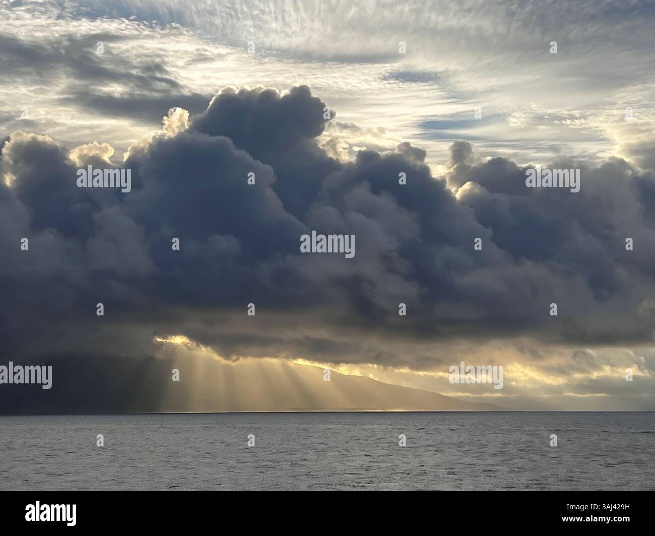 Sun rays break through heavy storm clouds over the ocean, casting golden light across the sea in ...